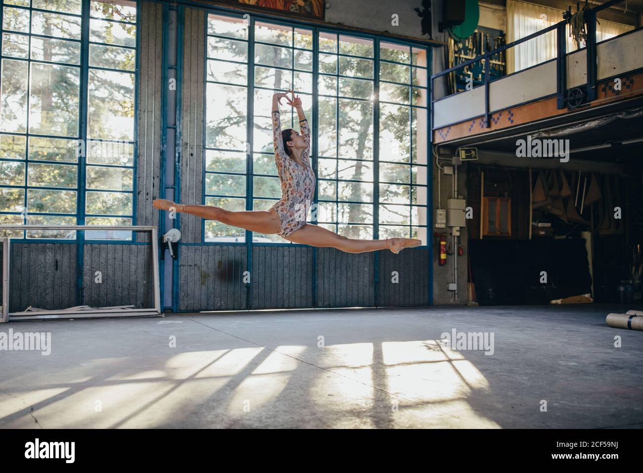 Side view of young slim ballerina in gymnastic suit jumping while ...