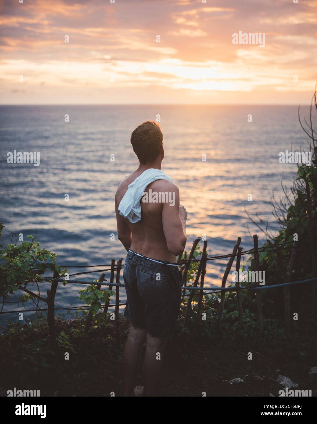 Side view of man standing alone on cliff at height looking at majestic ...