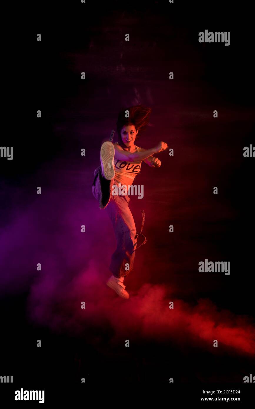 Modern female performing break dance on floor in purple and red smoke ...