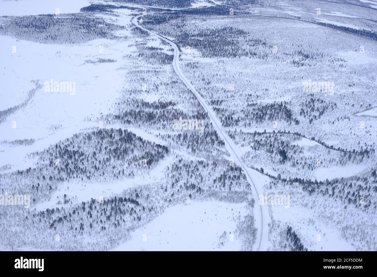 Drone view of narrow curvy road going through snowy fields and forests ...