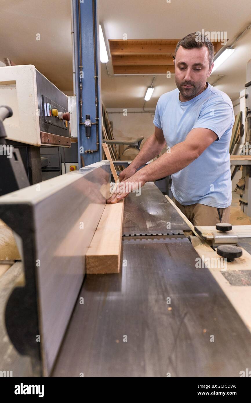 Male woodworker in casual clothes focusing and cutting lumber using ...