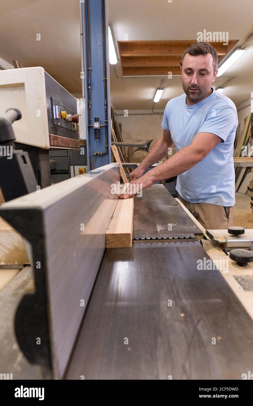 Male woodworker in casual clothes focusing and cutting lumber using ...