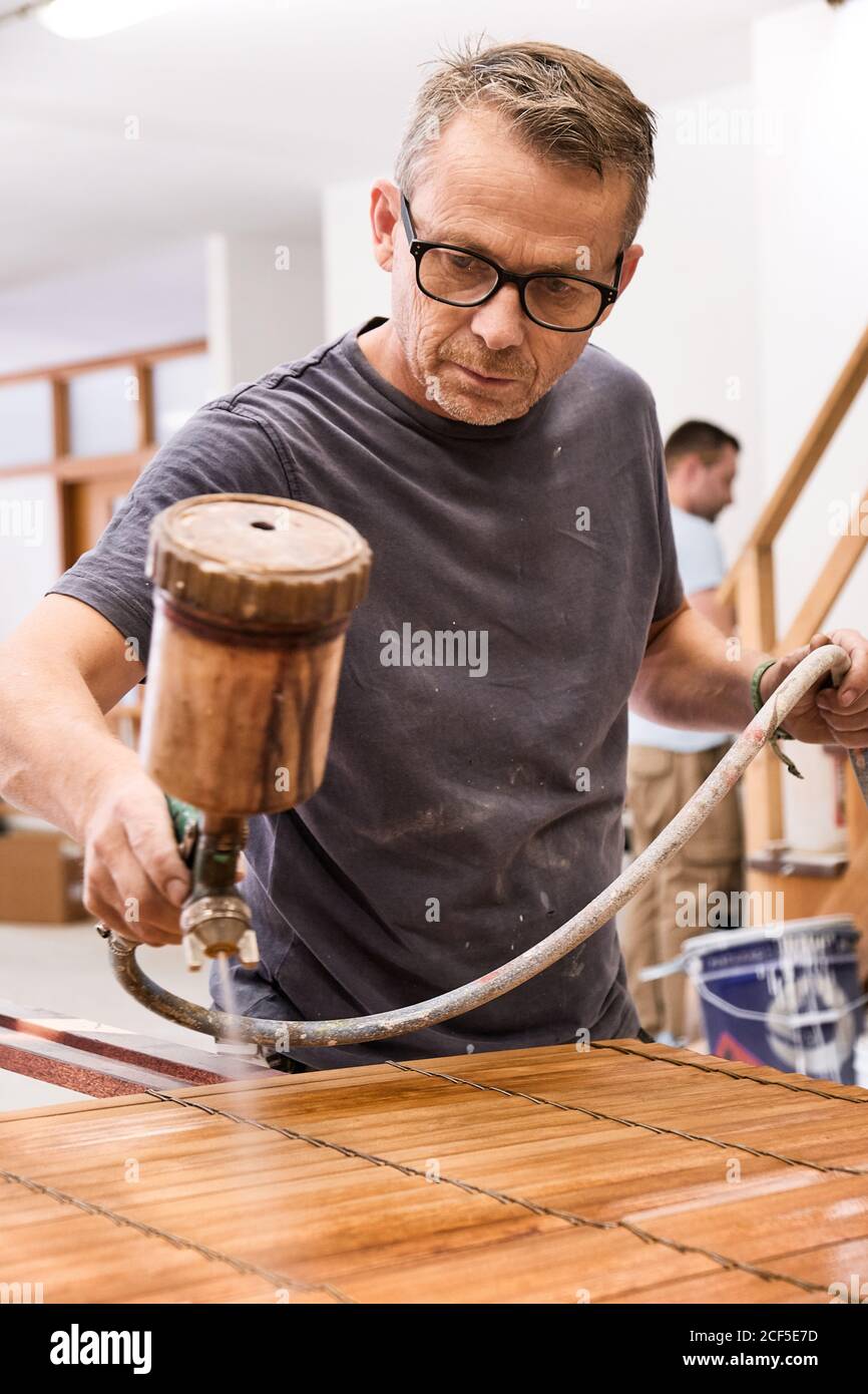 Craftsman applying varnish to wood jalousie using airbrush in carpentry ...