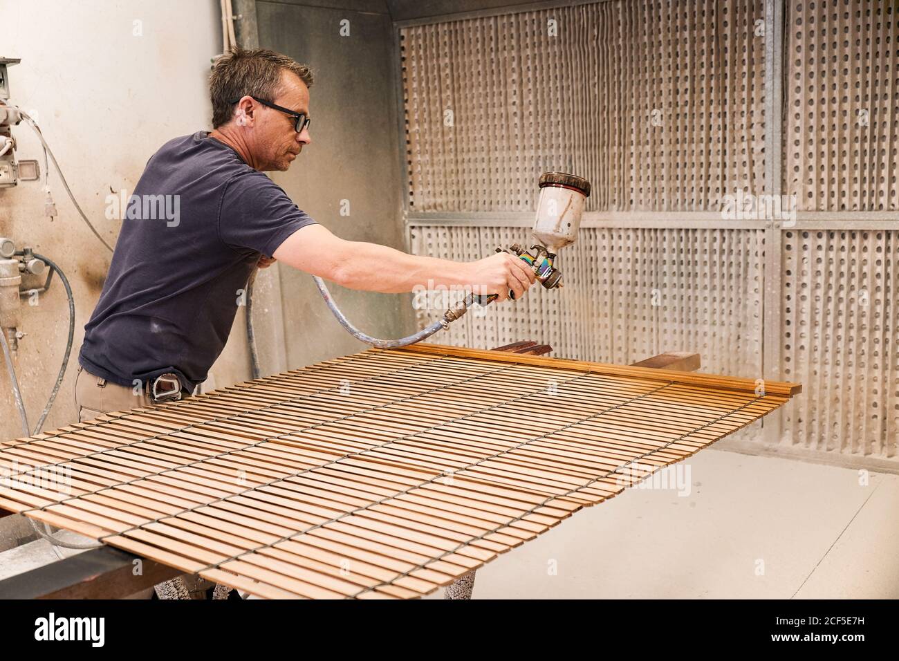 Adult focused man using spray gun painting wood slats with lacquer ...