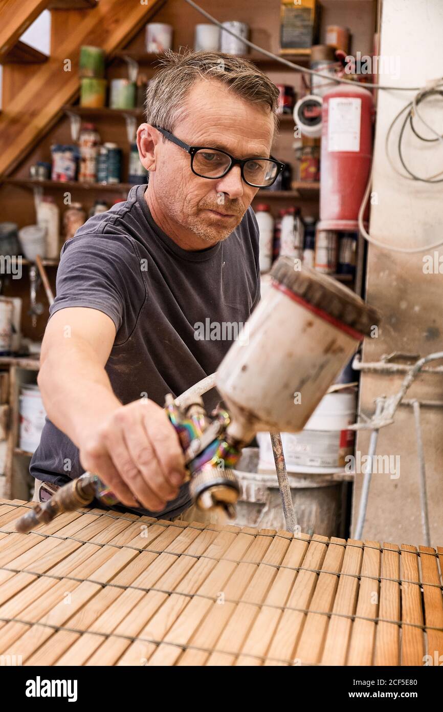 Craftsman applying varnish to wood jalousie using airbrush in carpentry ...