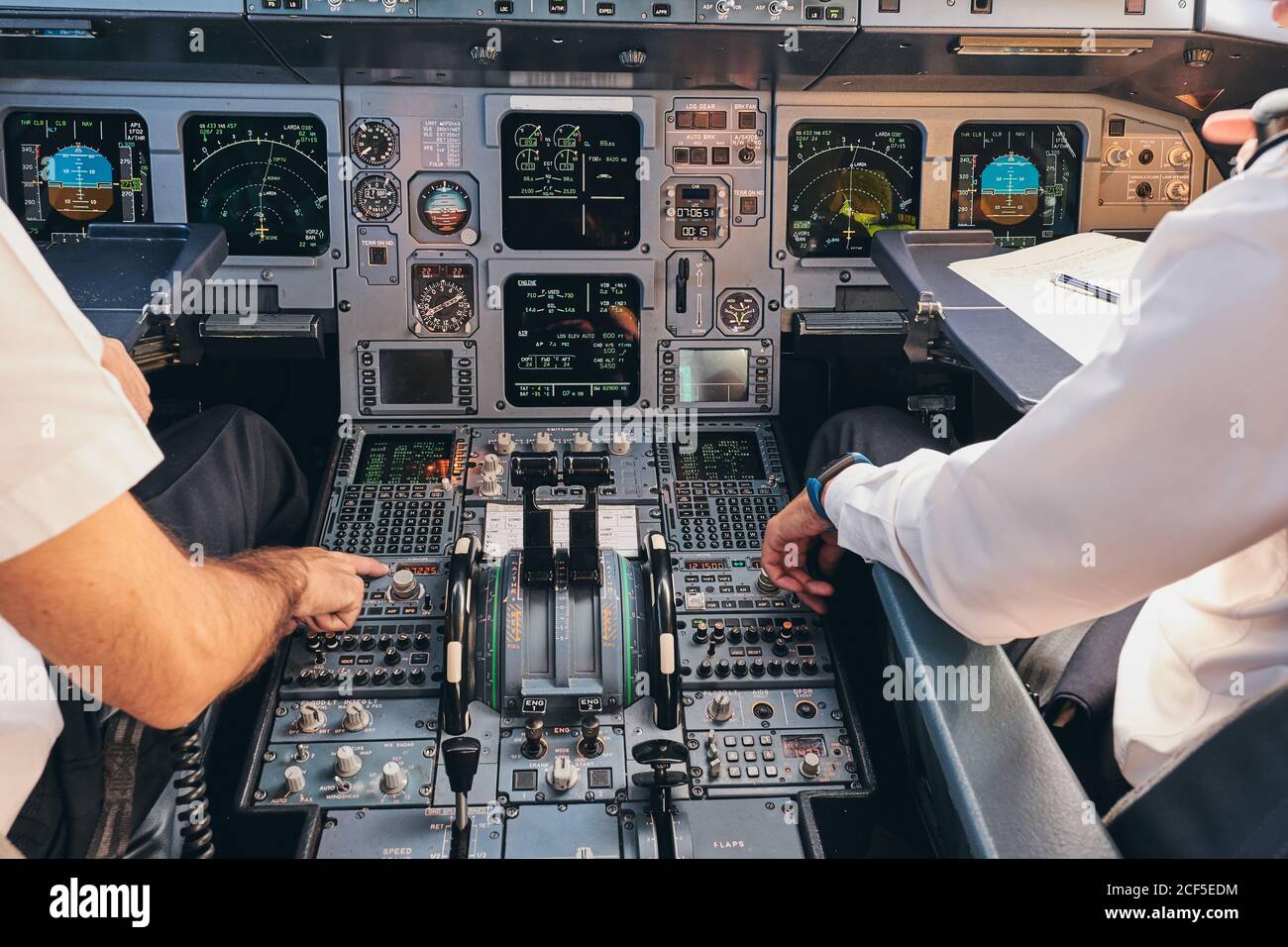 Back view of crop anonymous male captain and pilot sitting in cockpit of modern airplane and ...