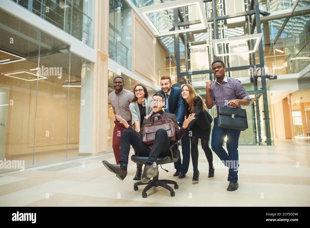Full length of young businesspeoples pushing colleague in chair at ...