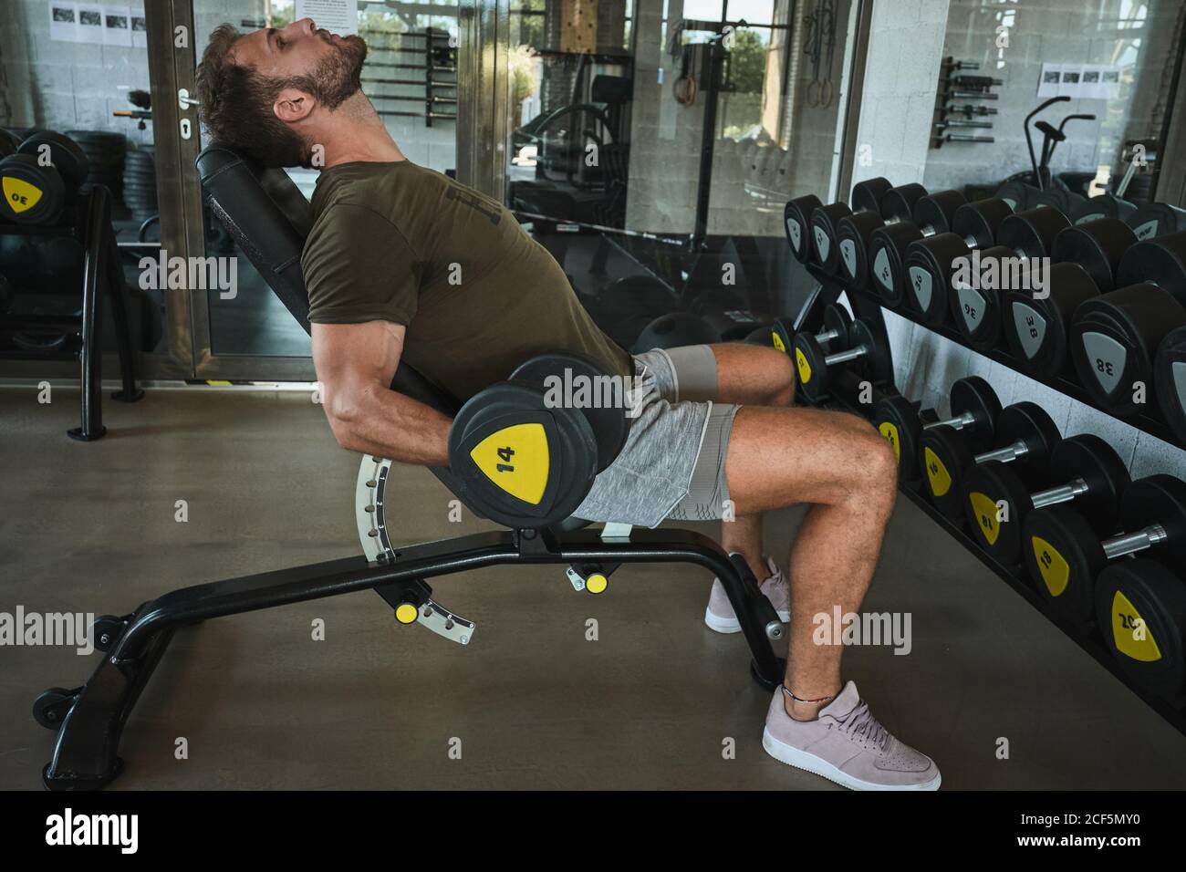 Side view of bearded muscular male in sportswear sitting on bench and ...