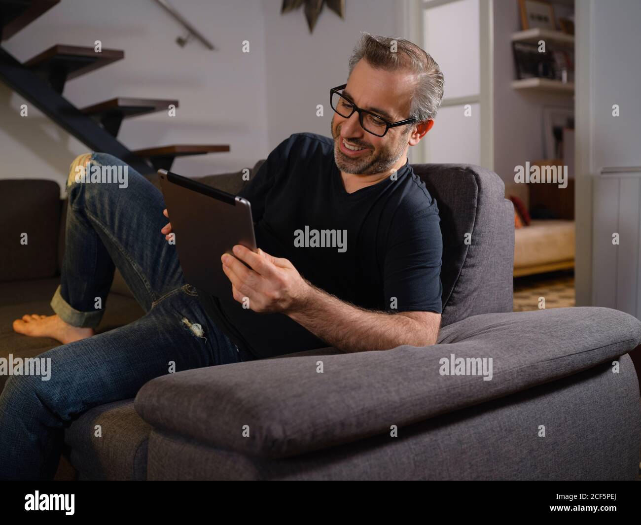 Relaxed man talking on the tablet serious alone on the sofa in the ...