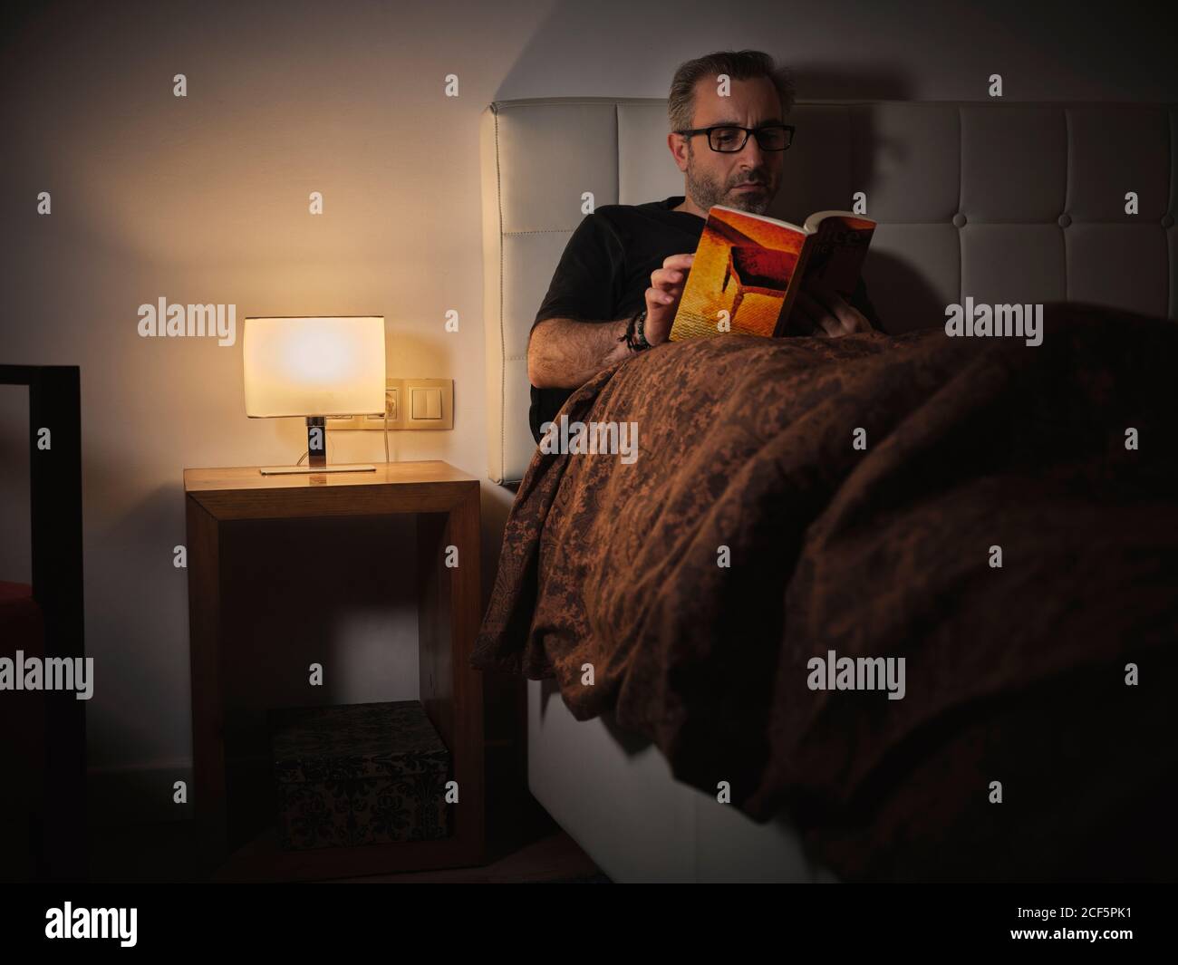 Relaxed man in bed reading a book before sleeping and resting Stock ...