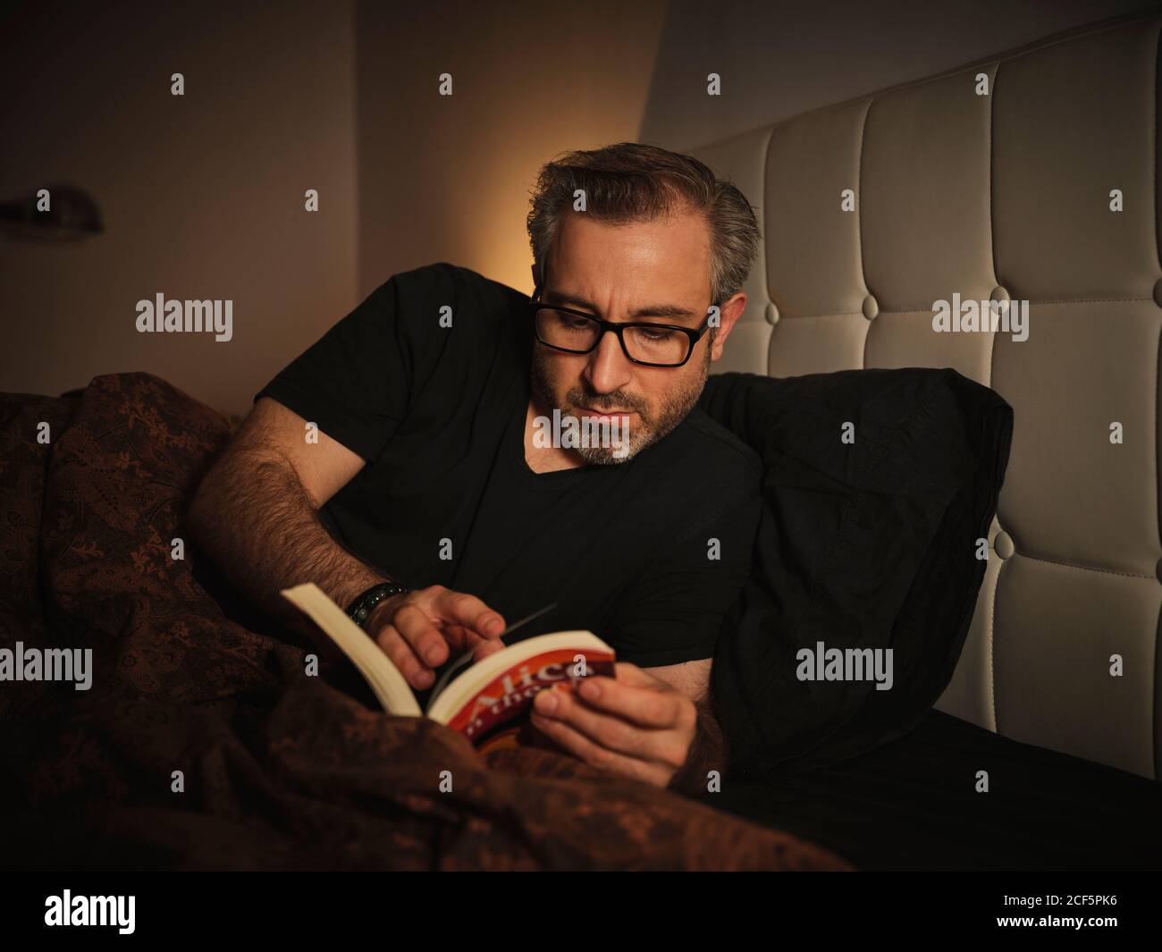 Relaxed man in bed reading a book before sleeping and resting Stock ...