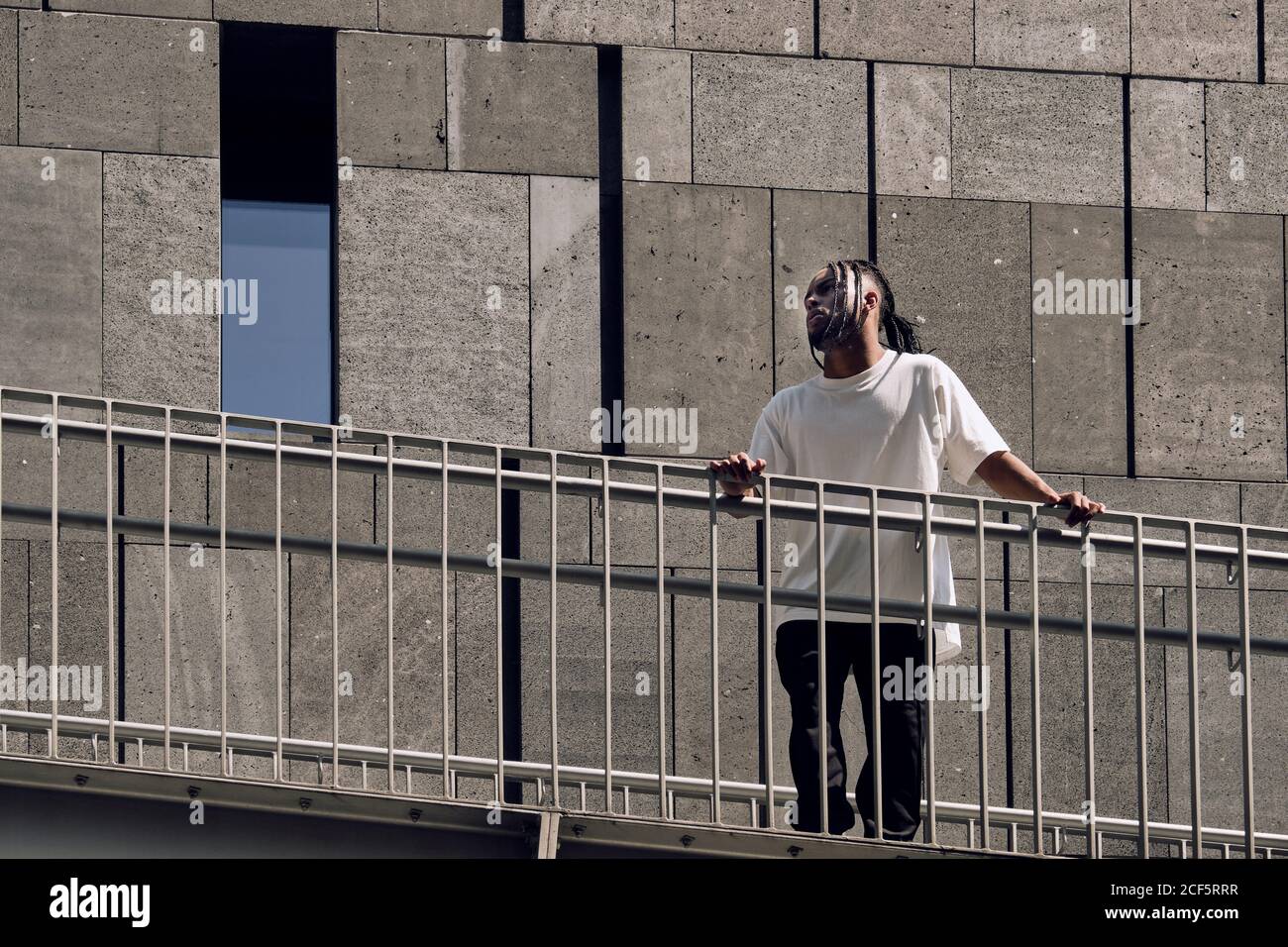 Young African American man leaning on railing of bridge while spending ...