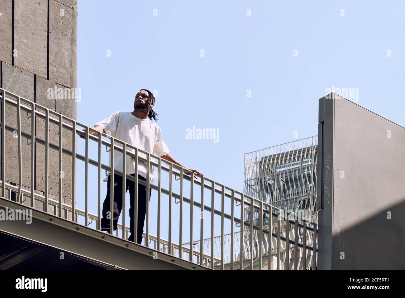 Young African American man leaning on railing of bridge while spending ...