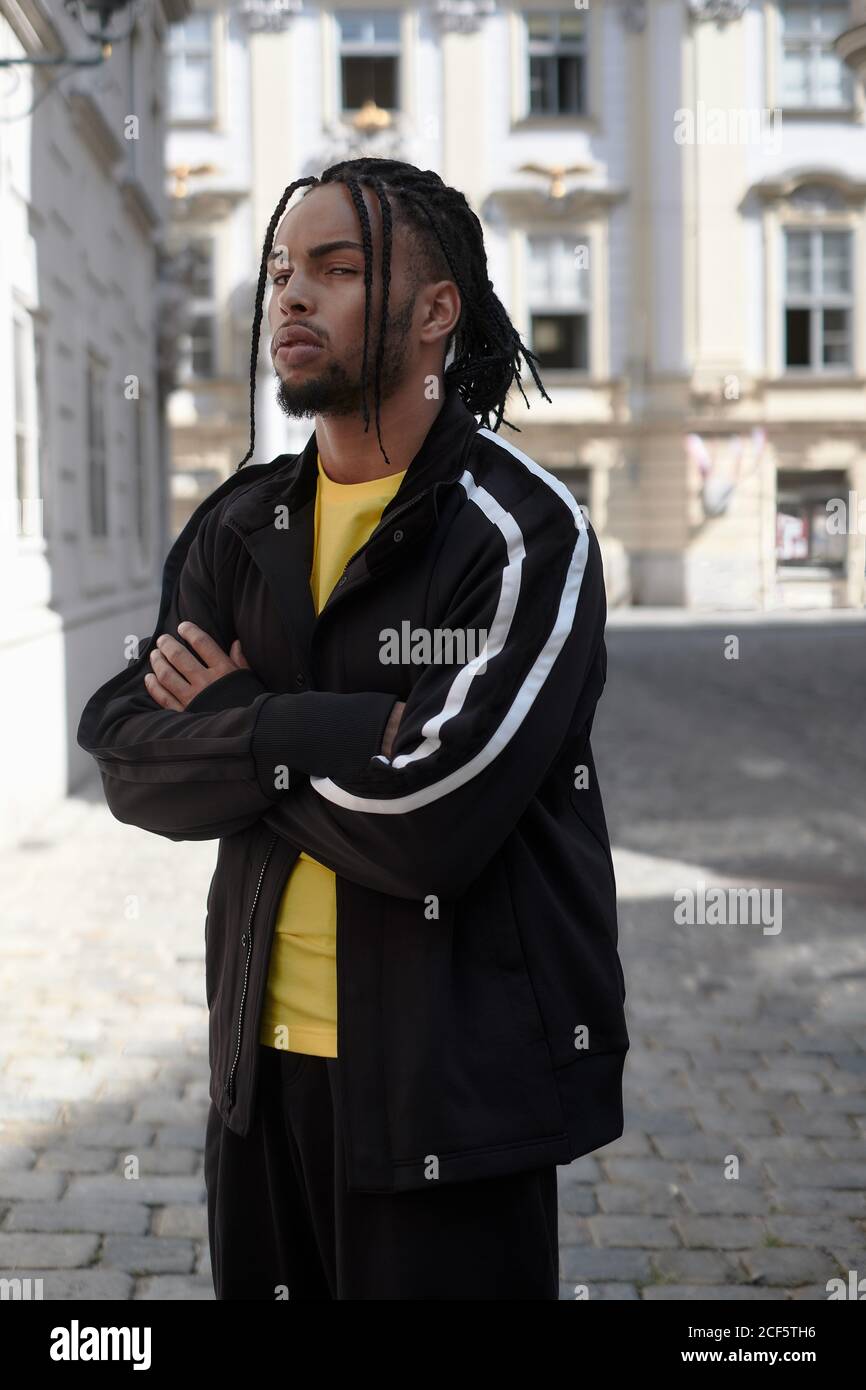 Young ethnic man with braided hair wearing black sports suit looking at ...