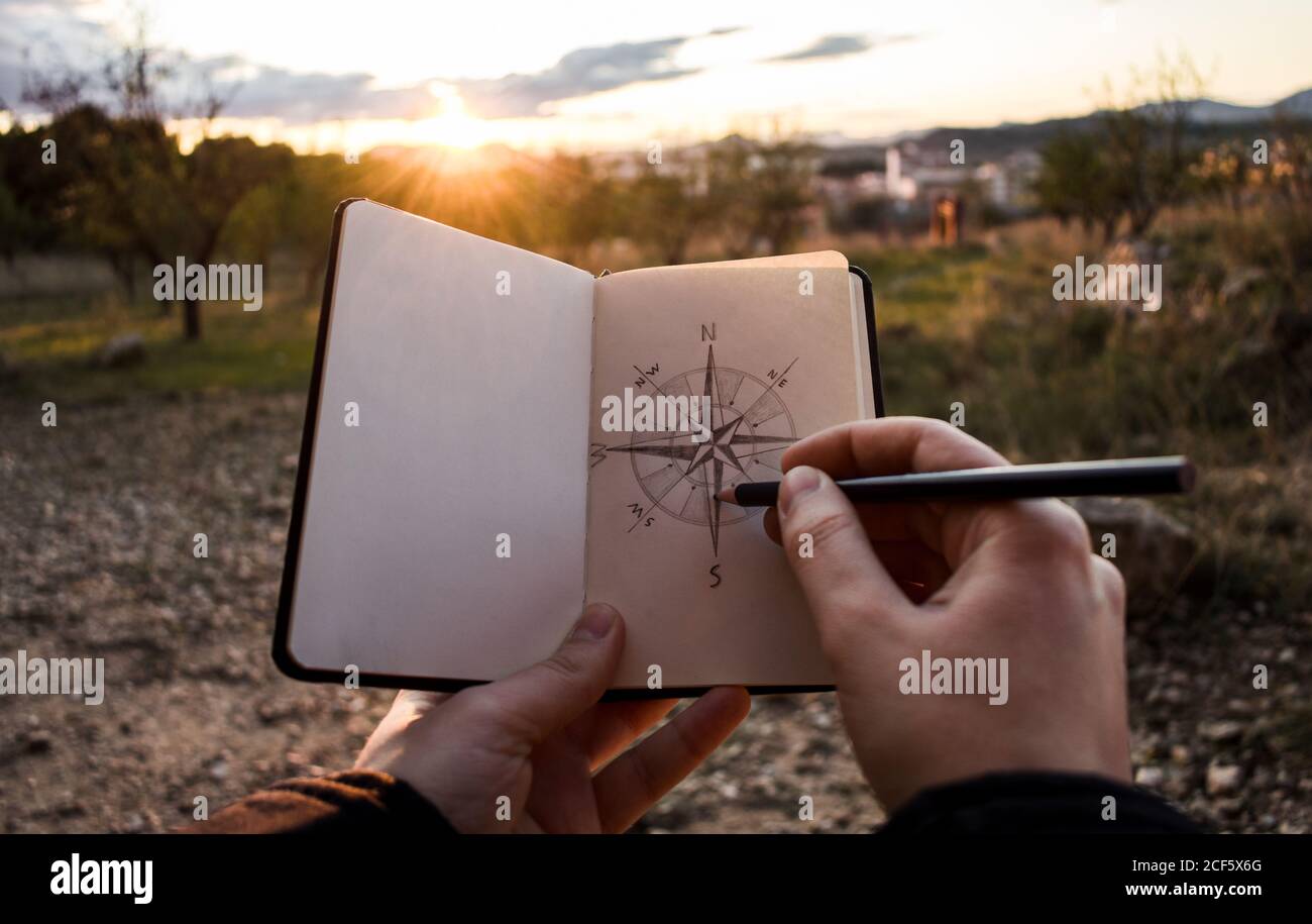 unrecognizable person drawing sketch of compass in notebook during trip ...