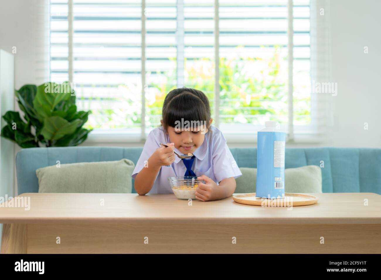 Asian elementary school student girl in uniform eating breakfast ...