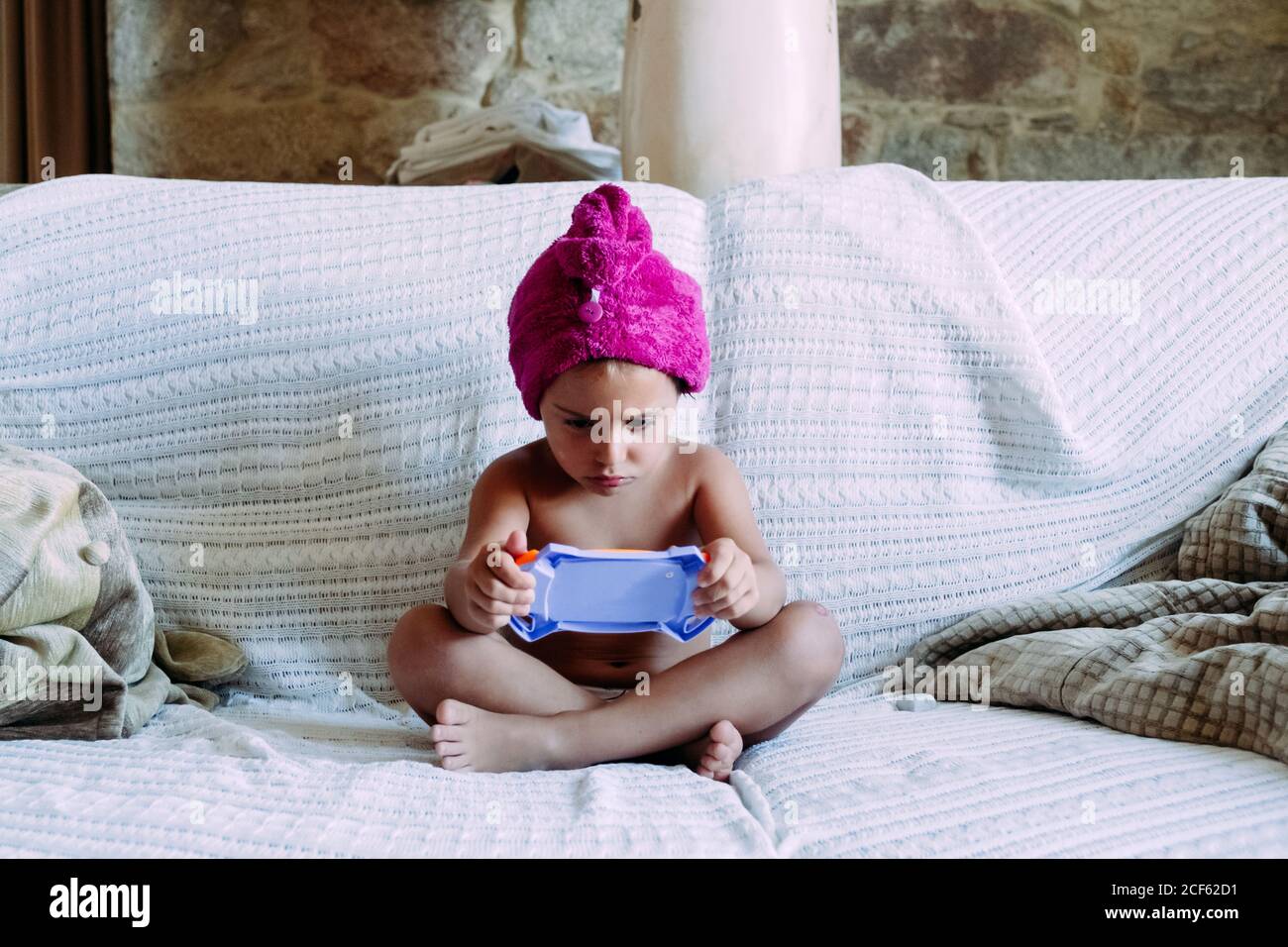 Kid in pink turban without clothes concentrated on playing with plastic ...