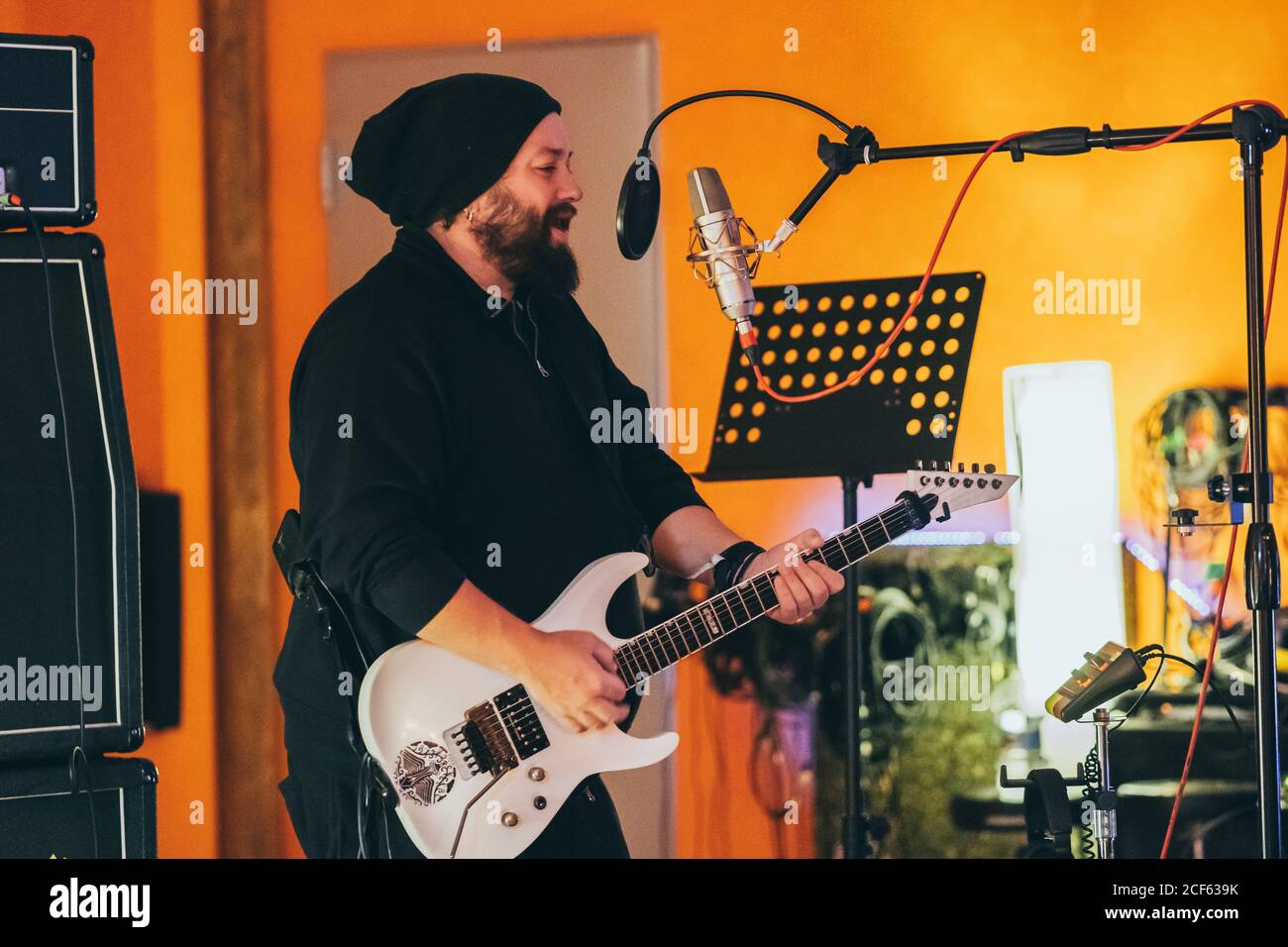 Adult man in music studio playing a guitar and singing in a microphone ...