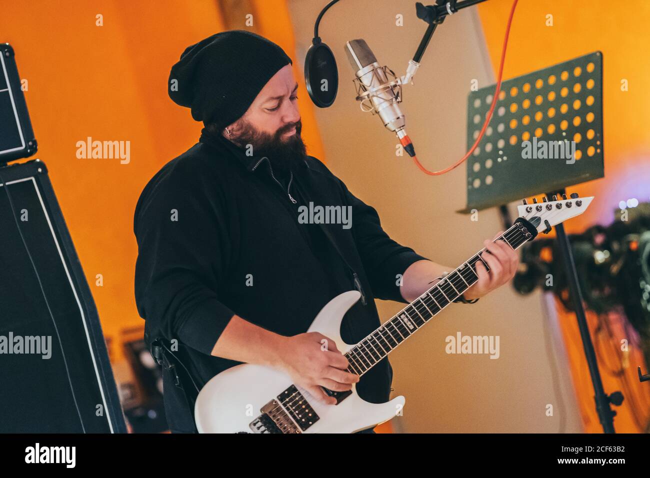 Adult man in music studio playing a guitar and singing in a microphone ...