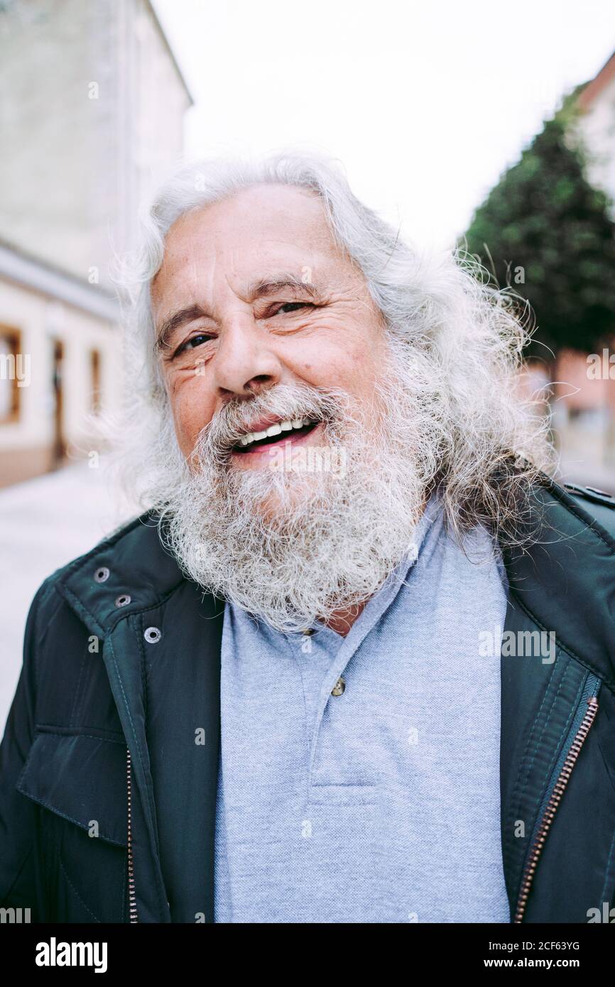 Happy senior male pensioner in casual wear smiling at camera while ...