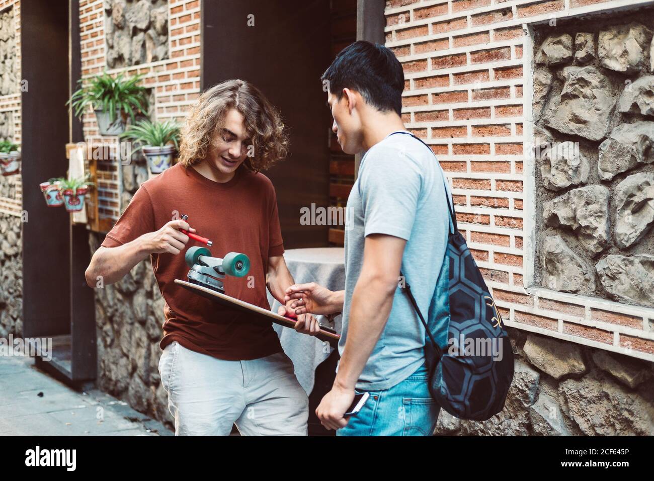Attentive men in casual outfit talking and holding longboard while ...