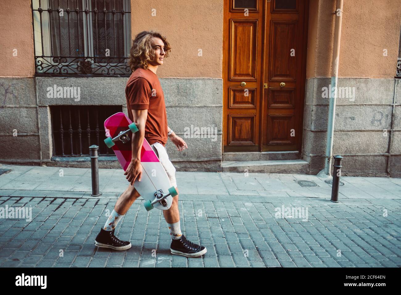 Side view of handsome sportive man holding longboard while walking on ...