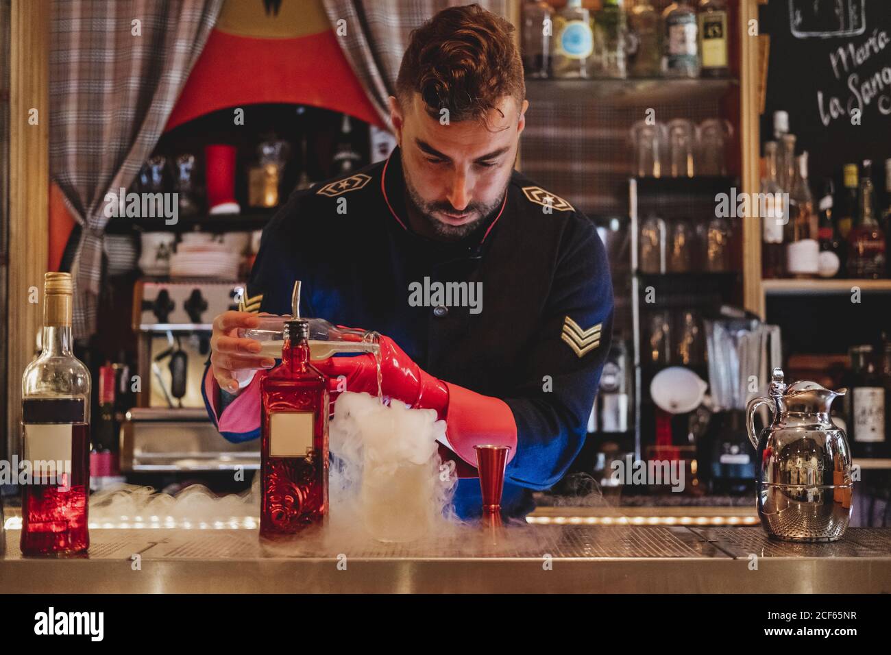 Barman in uniform and red gloves concentrated on preparing cocktail and ...