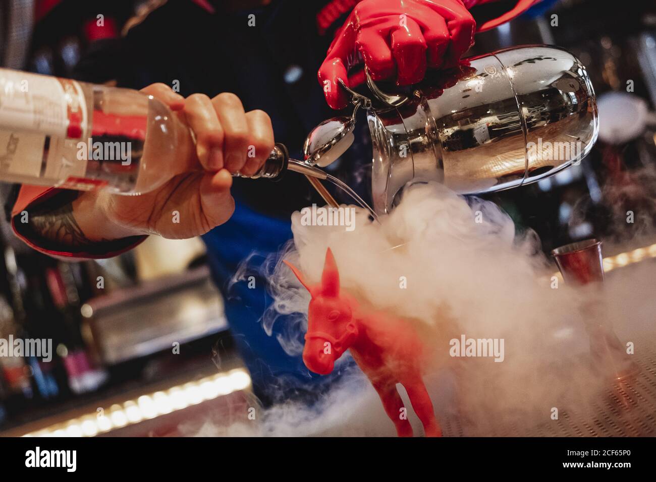 unrecognizable barman in uniform and red gloves concentrated on ...