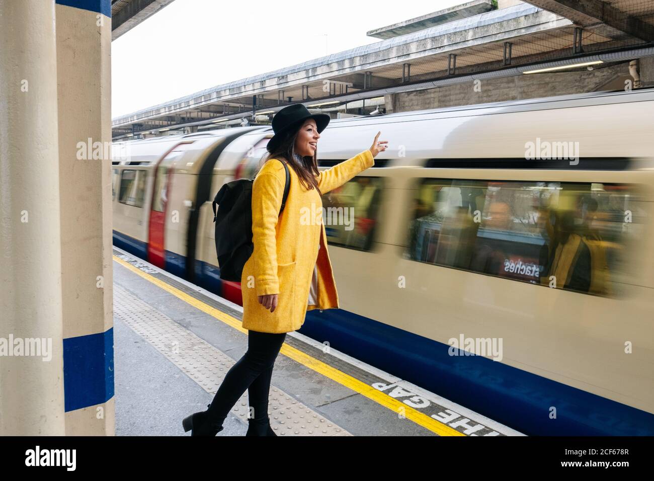 Side view of happy stylish female smiling and waiving hand near train ...