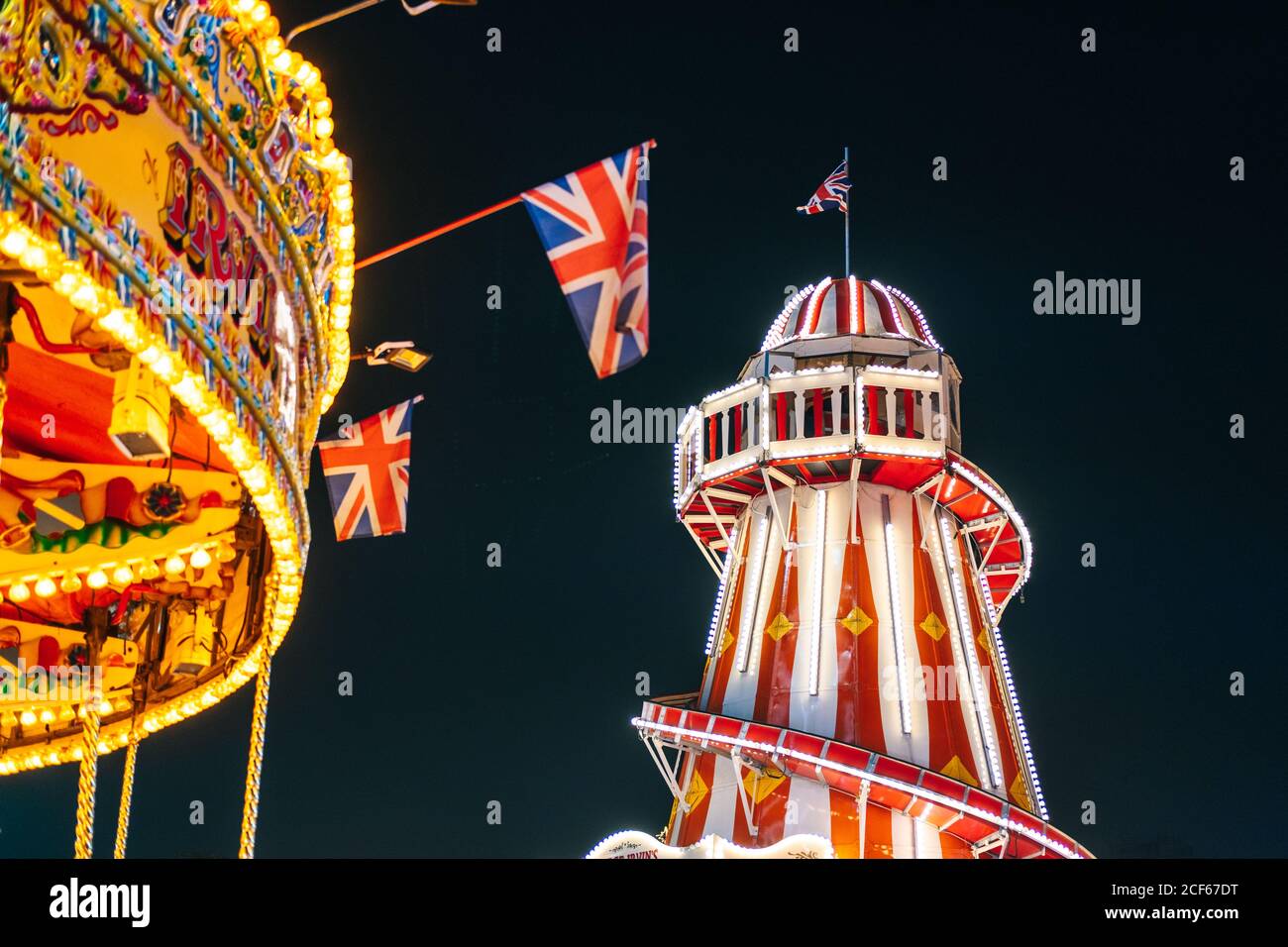 From below brightly illuminated rides with flags against dark night sky ...