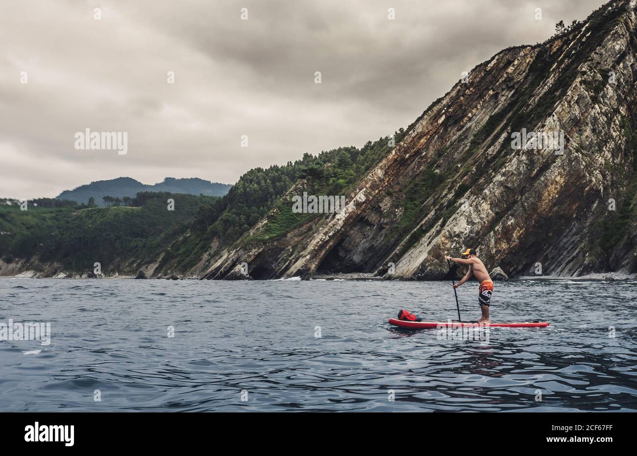 Adult male standing on paddleboard and rowing with paddle on surface of ...