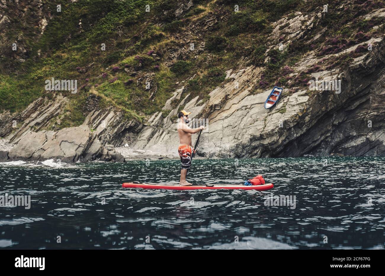 Adult male standing on paddleboard and rowing with paddle on surface of ...