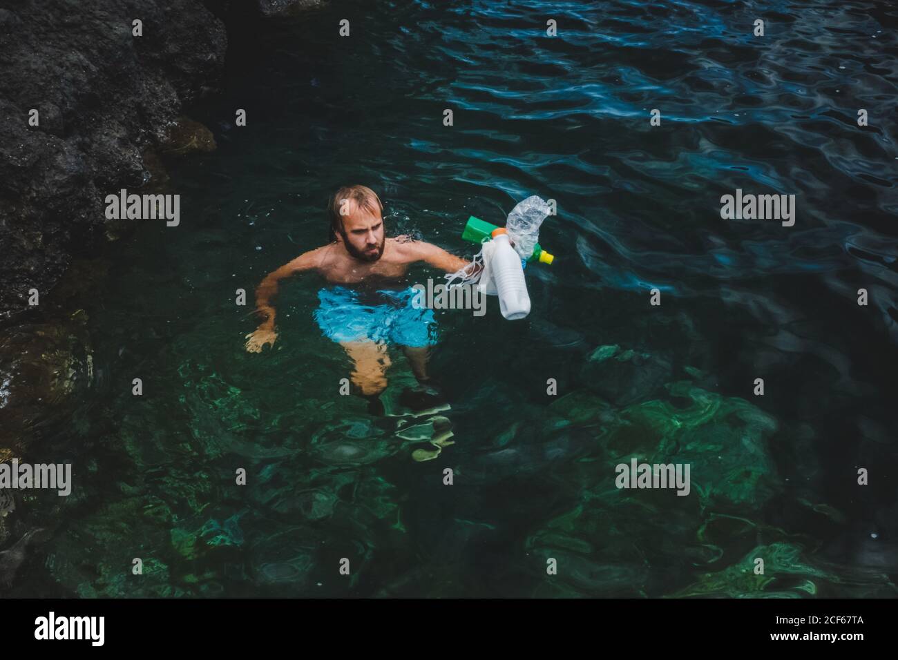 Sad man swimming in polluted water reservoir next to floating plastic ...