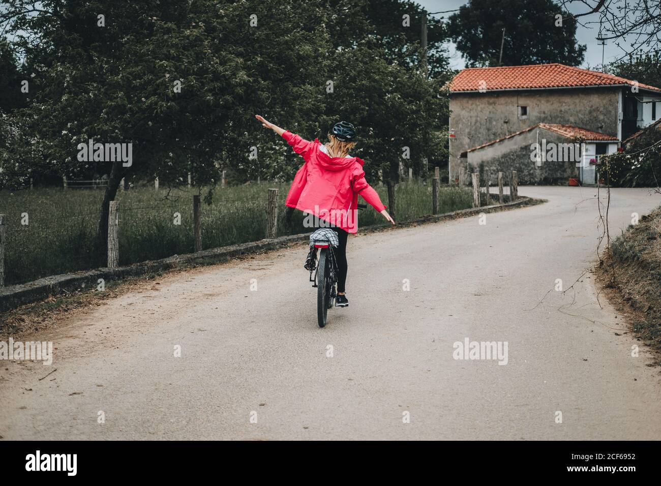 Back view of Woman balancing while cycling without hands on countryside ...