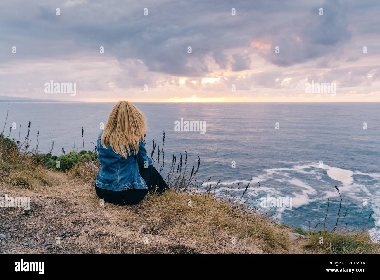 Back view of blond Woman chilling and contemplating scenic seascape ...