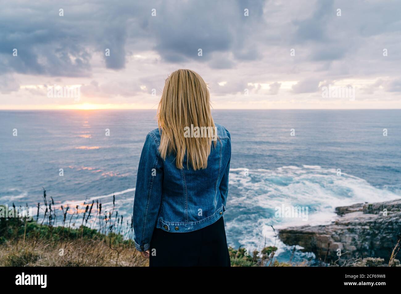 Back view of blond Woman chilling and contemplating scenic seascape ...