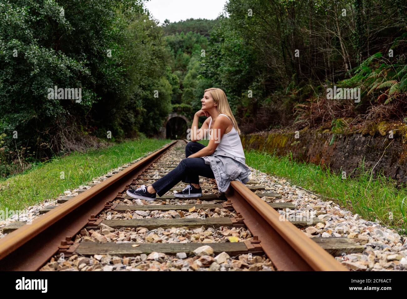 Woman sitting on railway though greenery part of road Stock Photo - Alamy