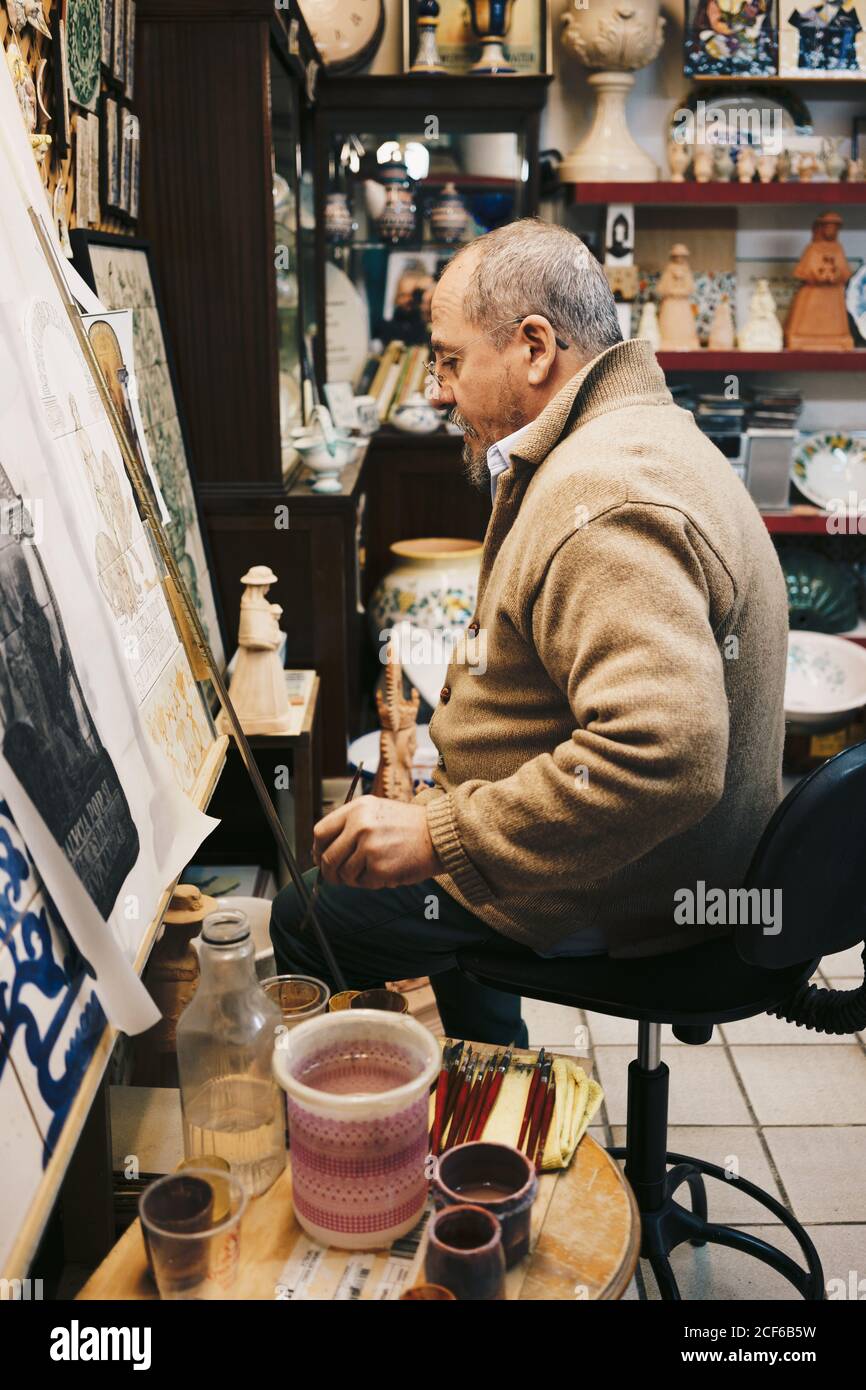 Side view of senior master working with ceramic tile on paint easel ...