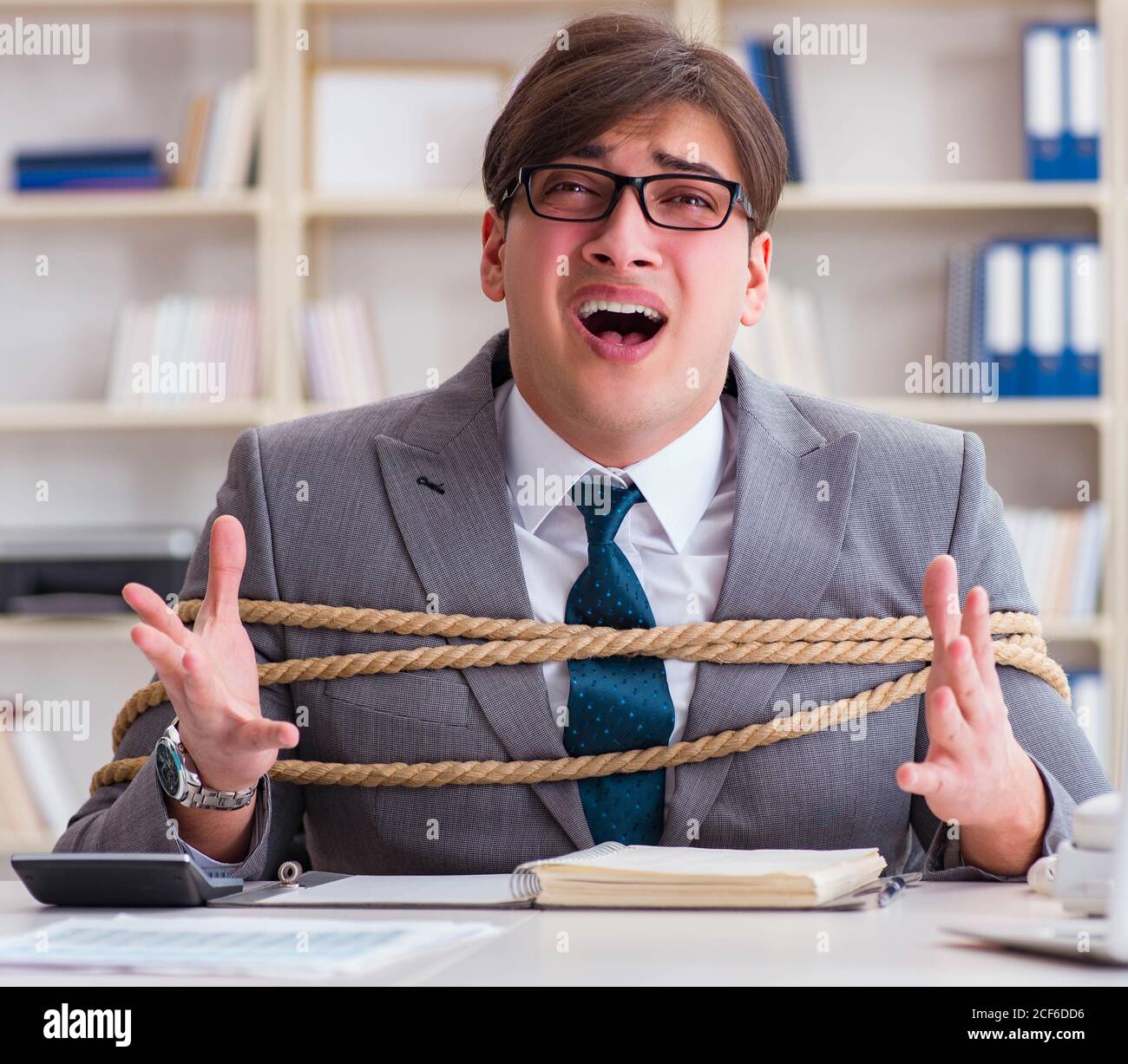 Businessman tied up with rope in office Stock Photo - Alamy