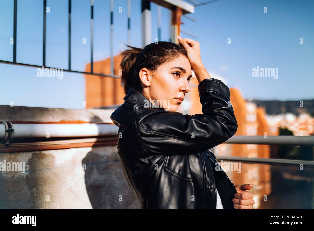 Side view of serene female in trendy leather jacket standing on summer ...
