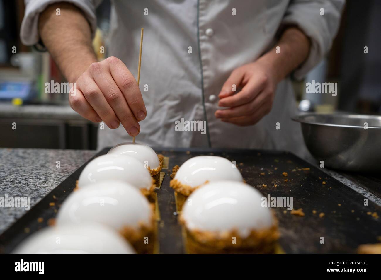 Crop person putting a wooden stick into cakes arranged on metal board ...