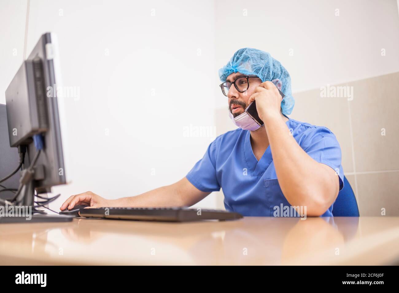 male surgeon using her computer and his smartphone in her office before ...