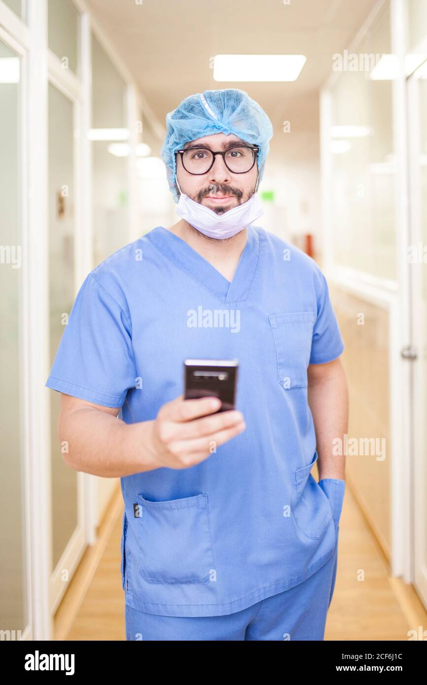 Male surgeon standing in the hallway while checking messages on his ...