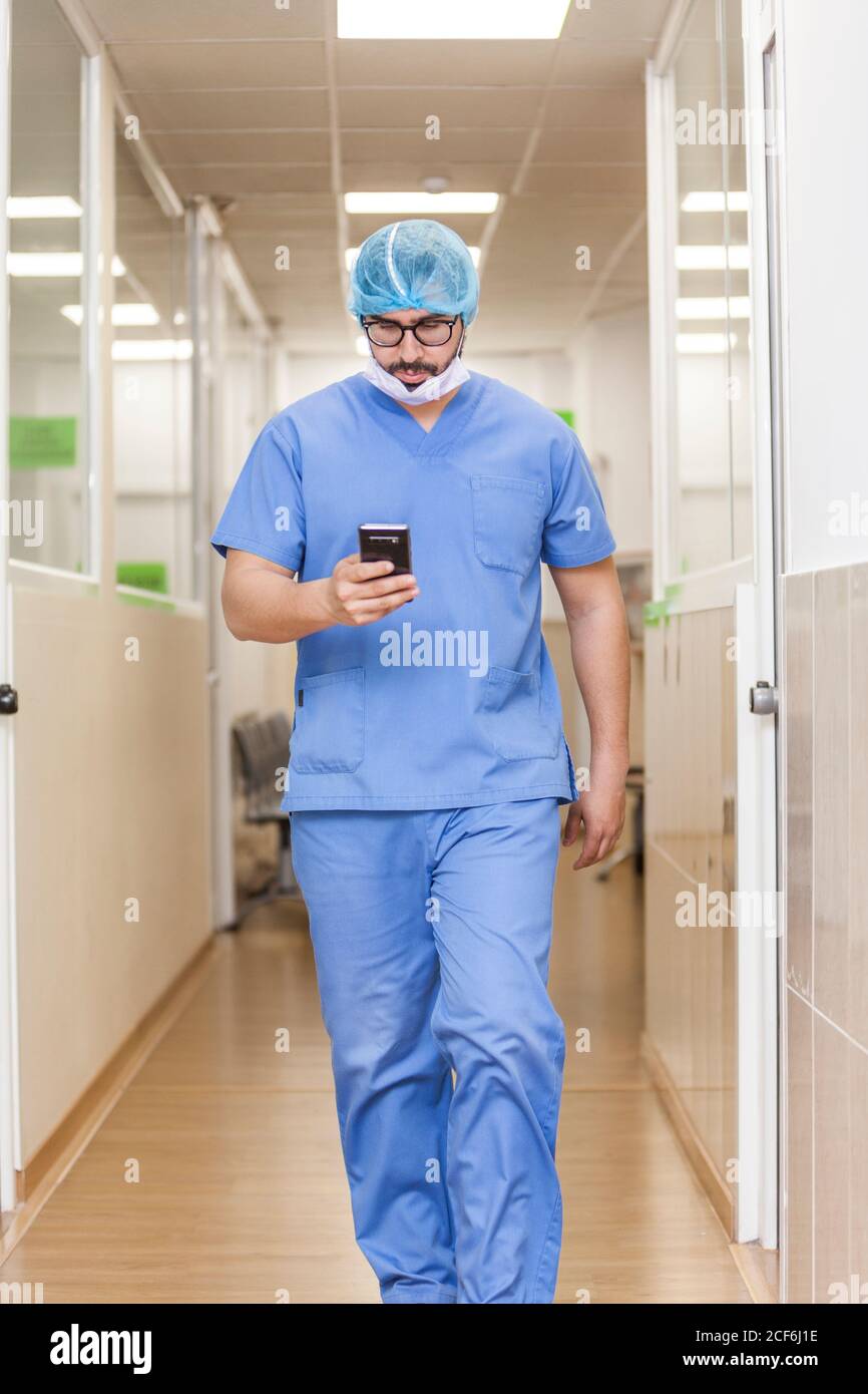 Male surgeon standing in the hallway while checking messages on his ...