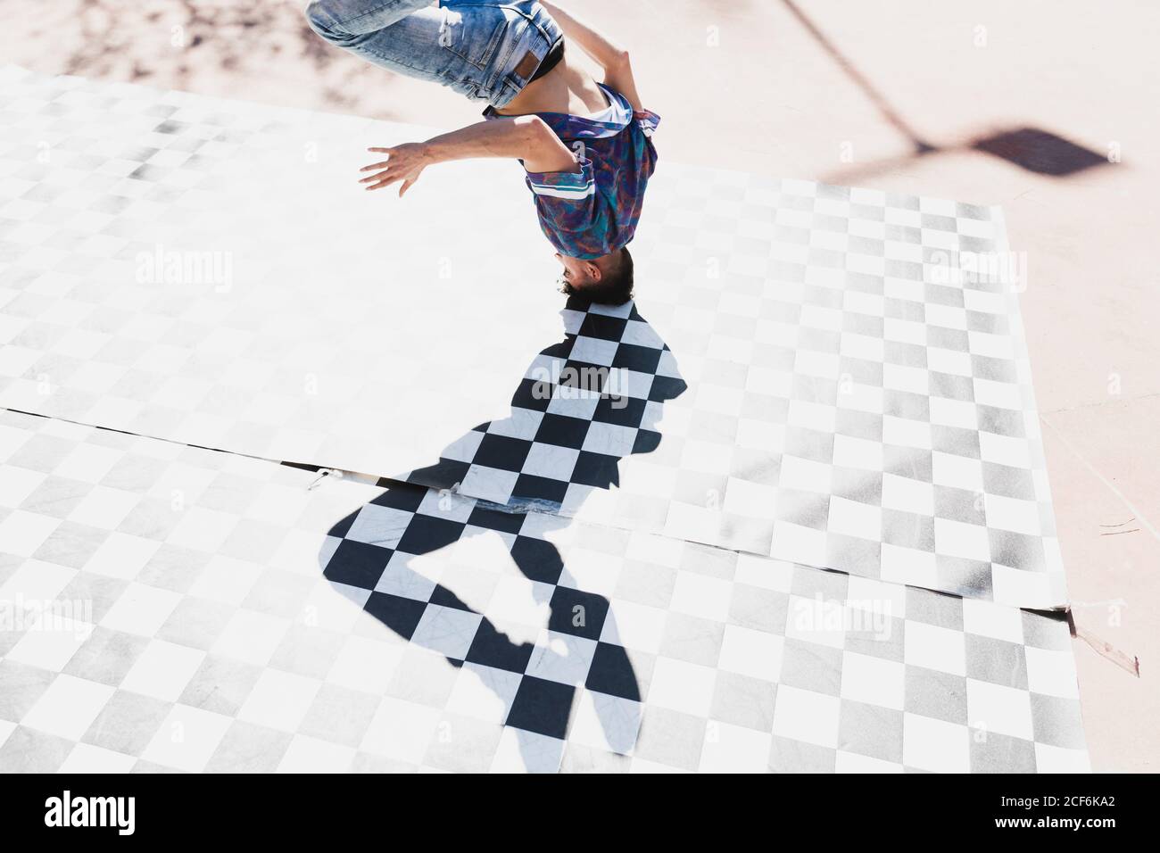 From above shadow of crop young guy doing headstand on checkered floor ...
