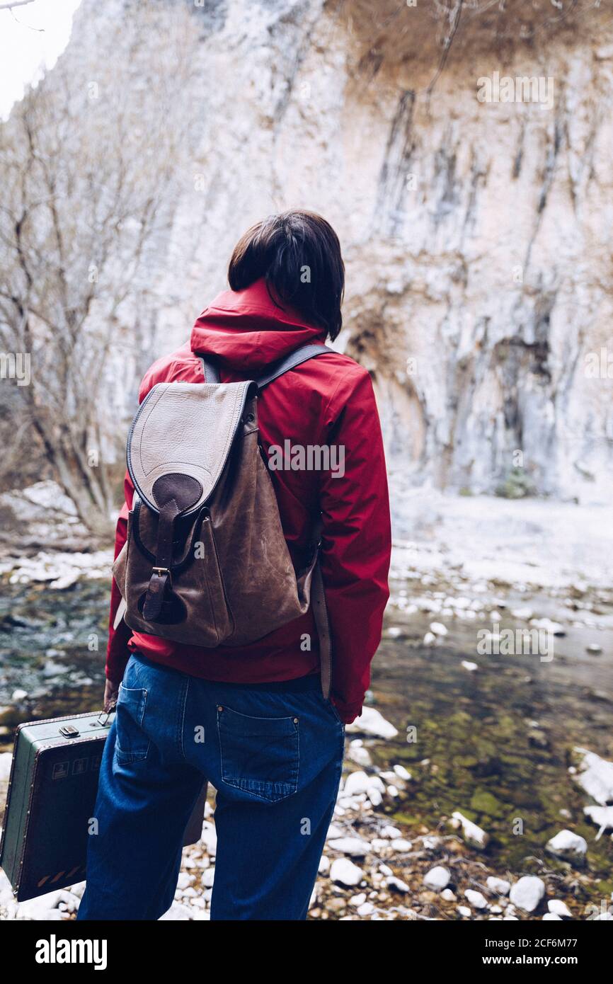 back view of casual Woman carrying case and jumping on rocks of clear ...