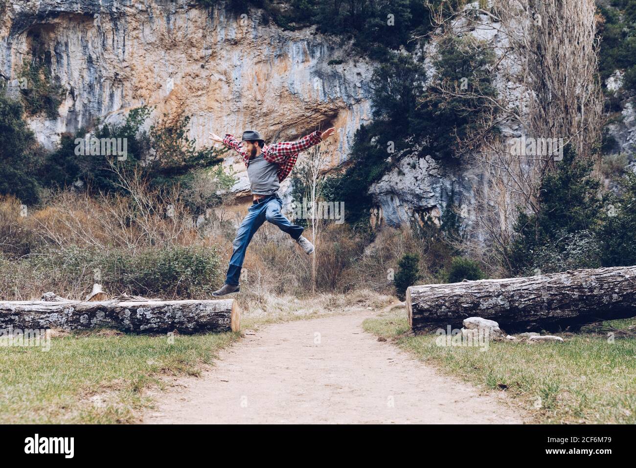 Casual man jumping among fallen trunks on rural road against beautiful ...