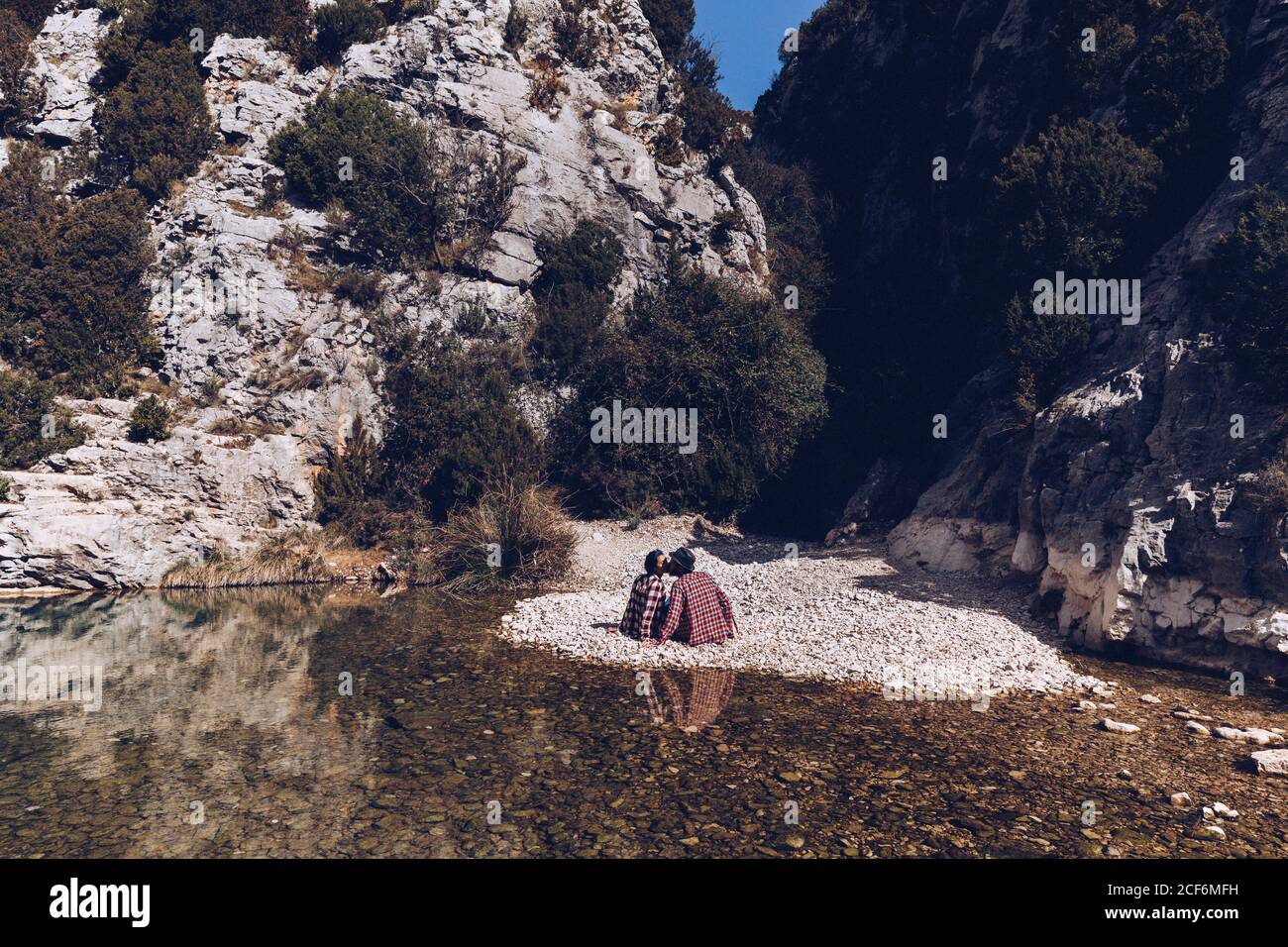 Back view of young couple sitting and kissing on rock coast of mountain ...
