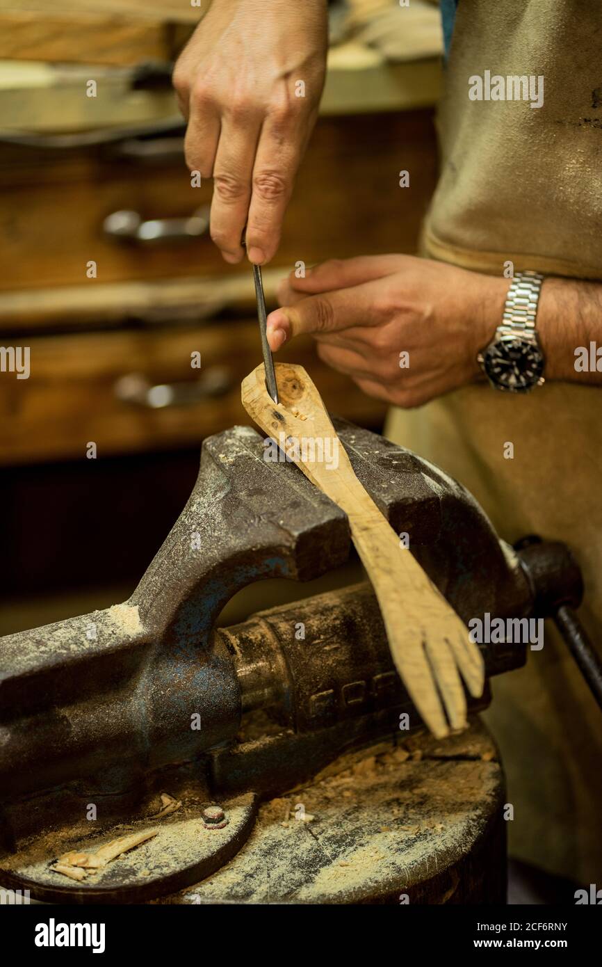Crop anonymous carpenter in apron using chisel for making hole in ...