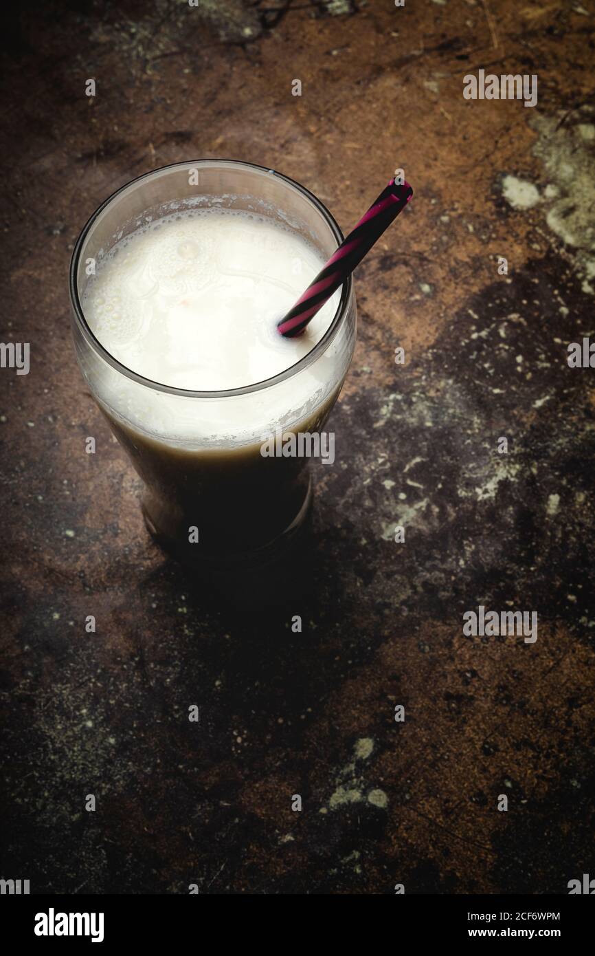 Tall glass of white milk with bright striped straw on table over black ...